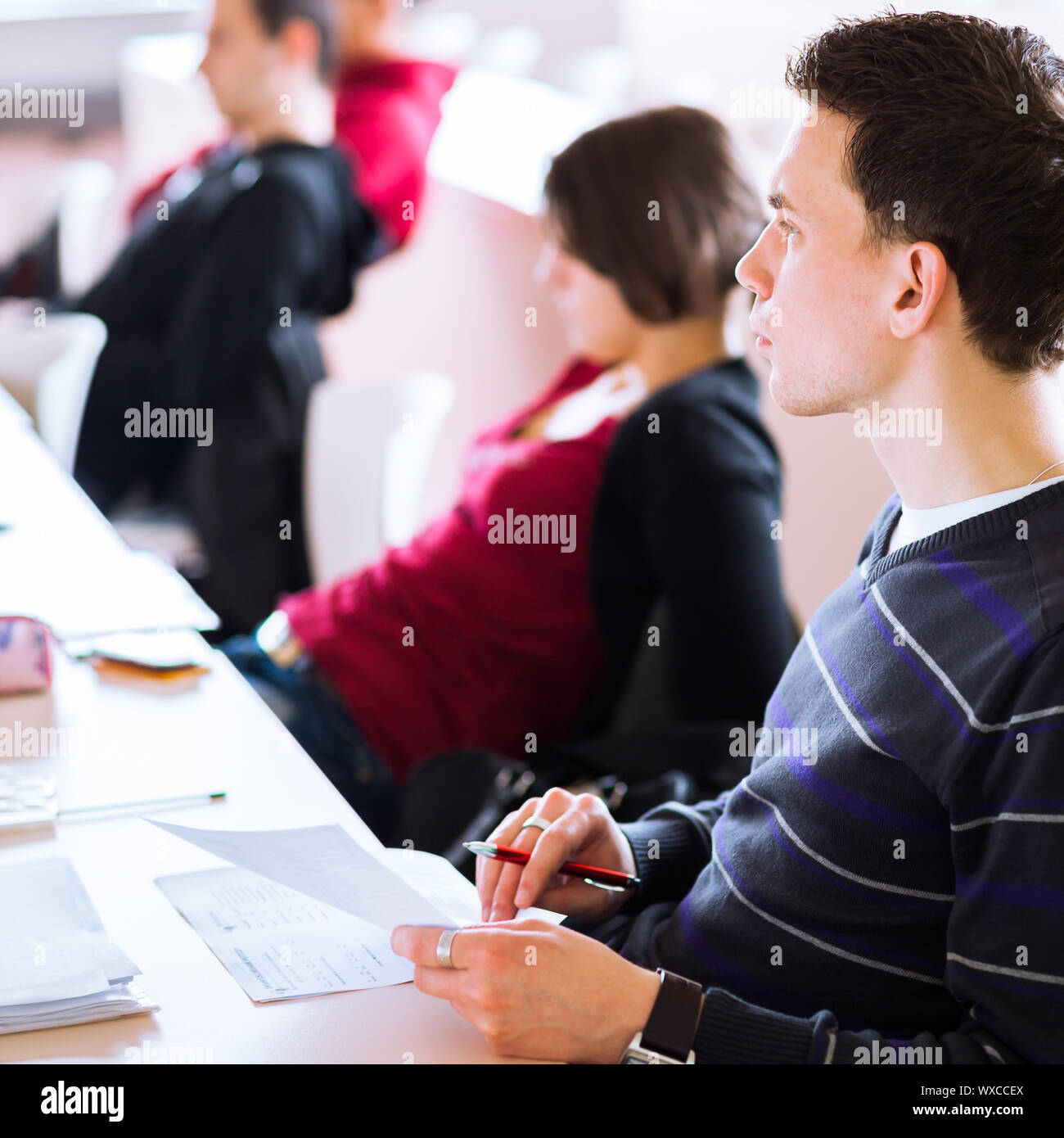 young, handsome male college student sitting in a classroom full of ...