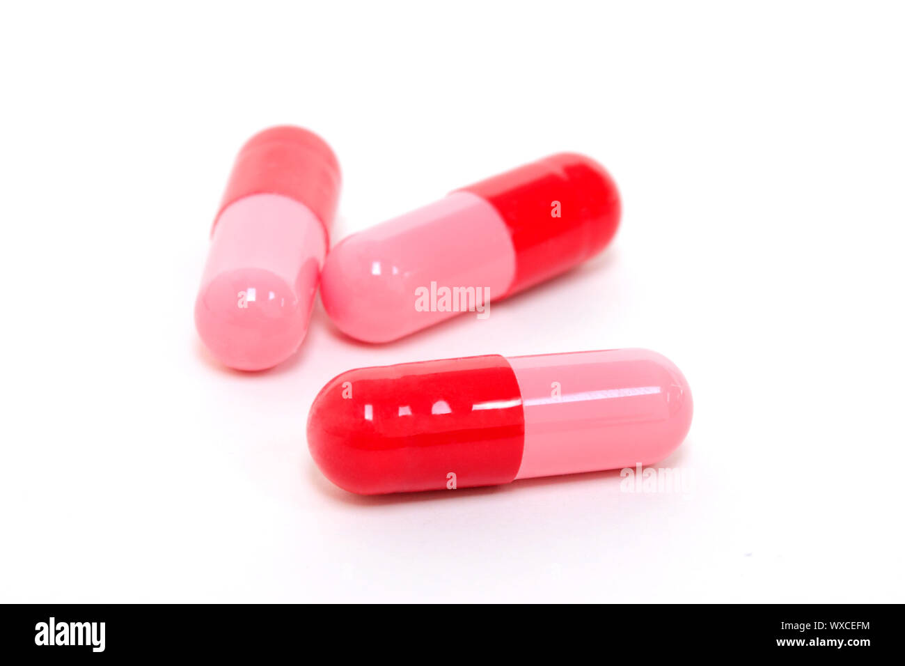 Red and pink colored capsules on white background Stock Photo - Alamy