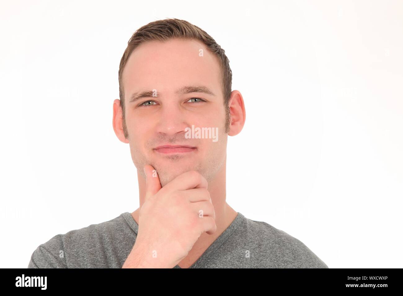 Happy thoughtful young man smiling as he stands with his hand to his ...