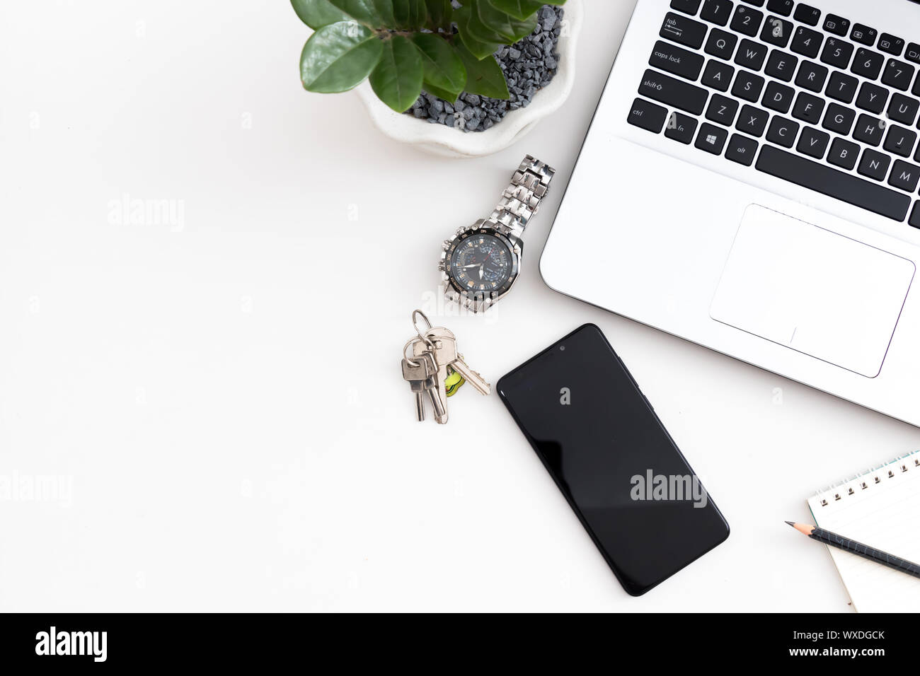 White office desk with laptop watch key office plant Stock Photo - Alamy