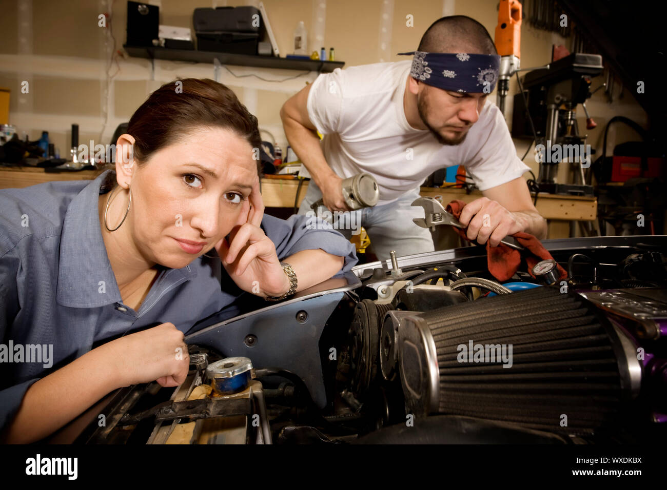 Bored woman leaning on car with male mechanic ignoring her in ...