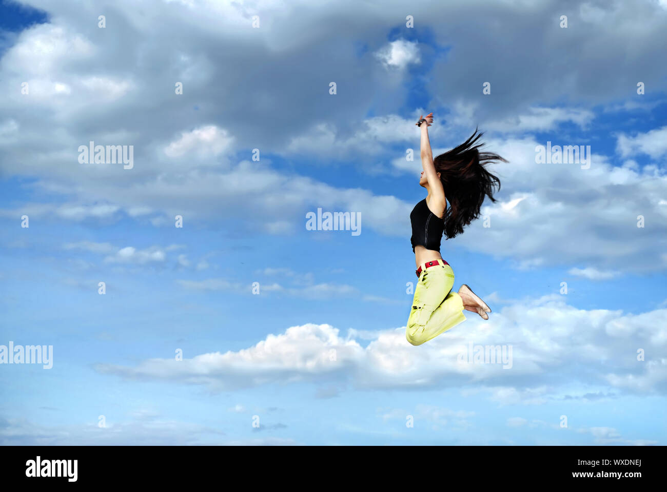 A young girl jumping in front of blue sky and clouds Stock Photo - Alamy