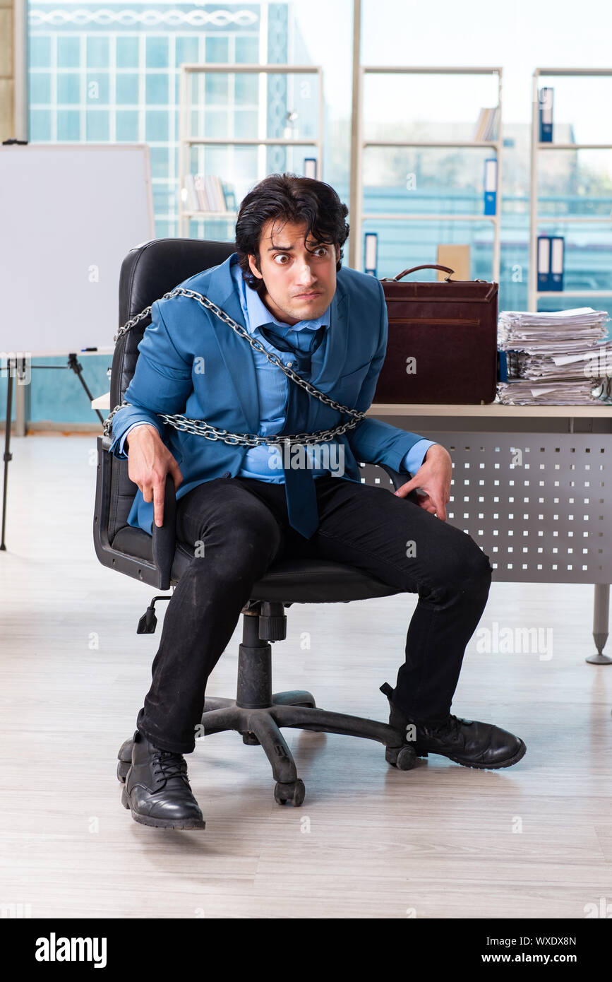 Chained male employee unhappy with excessive work Stock Photo - Alamy