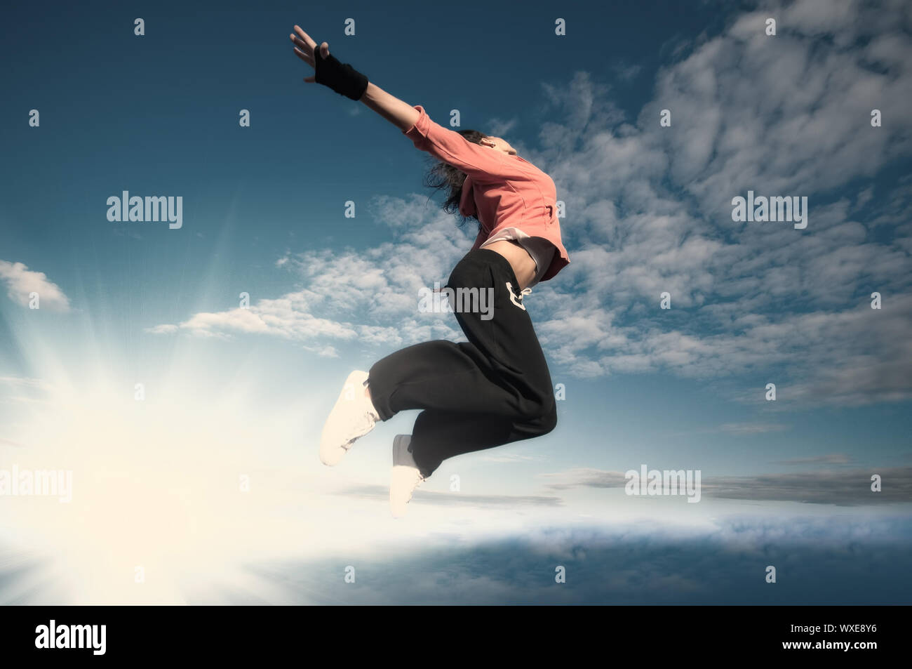 Beautiful sport woman in urban sportswear jumping and fly over blue sky ...