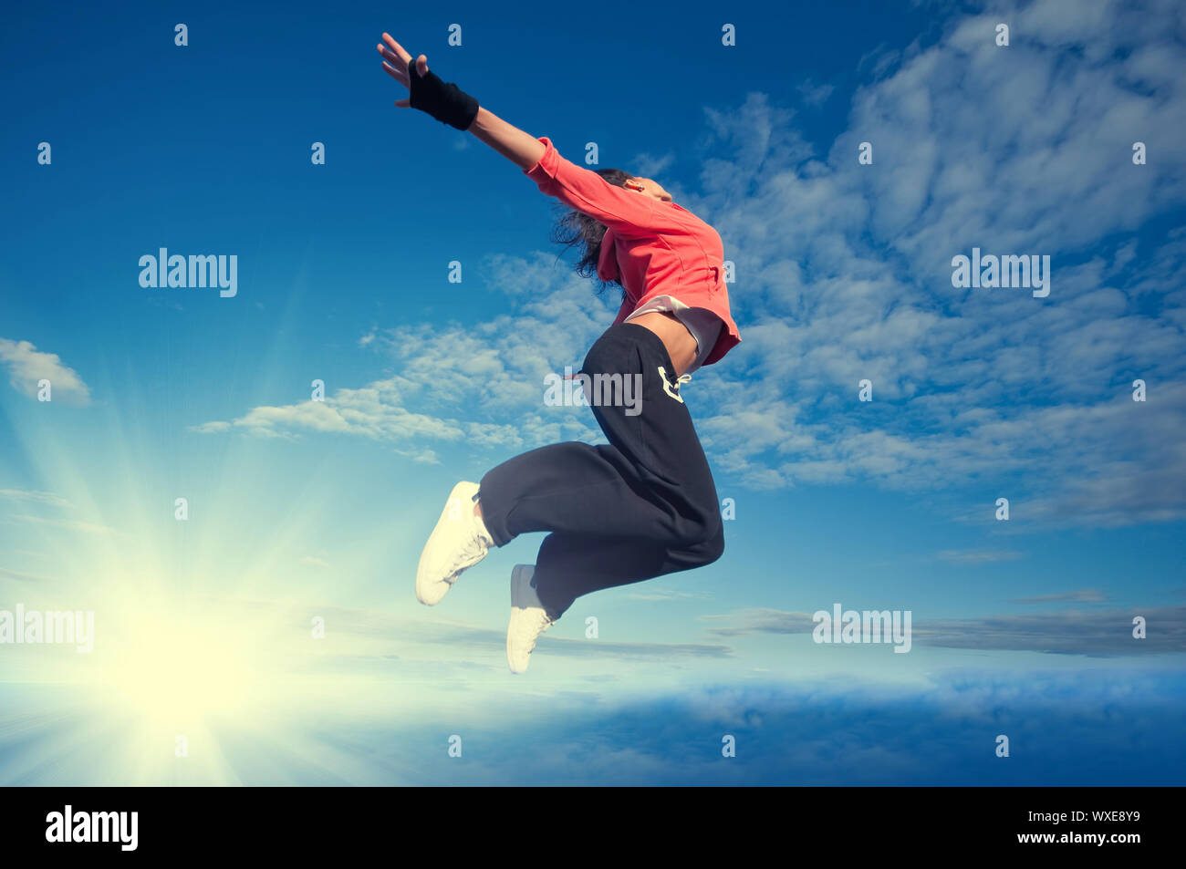 Beautiful sport woman in urban sportswear jumping and fly over blue sky ...