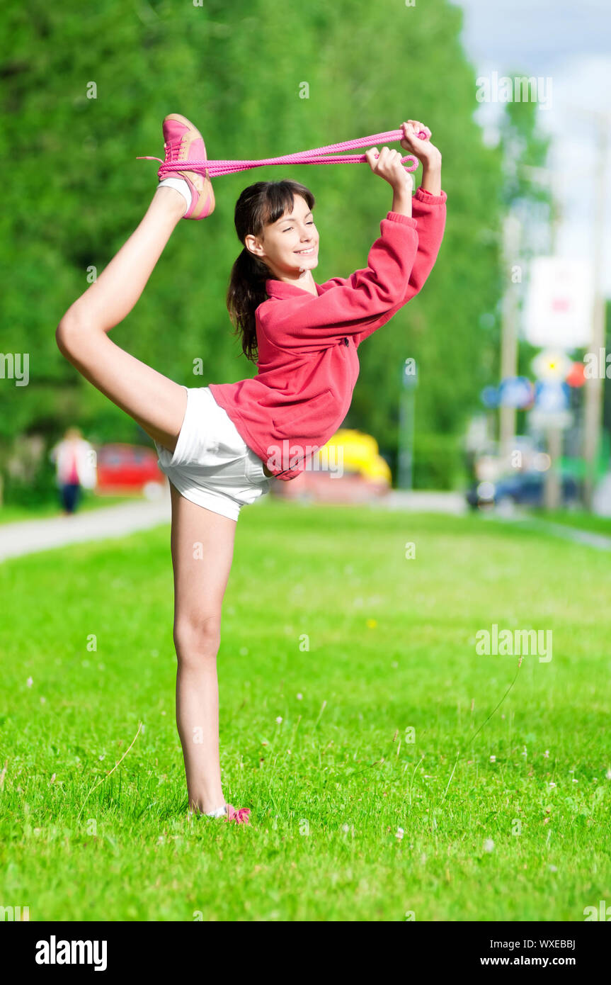 Teenage girl doing stretching exercise on green grass at park. Yoga ...