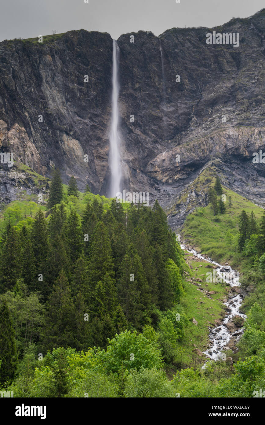 high waterfall plummets off a rock and grass cliff in the Swiss Alps ...