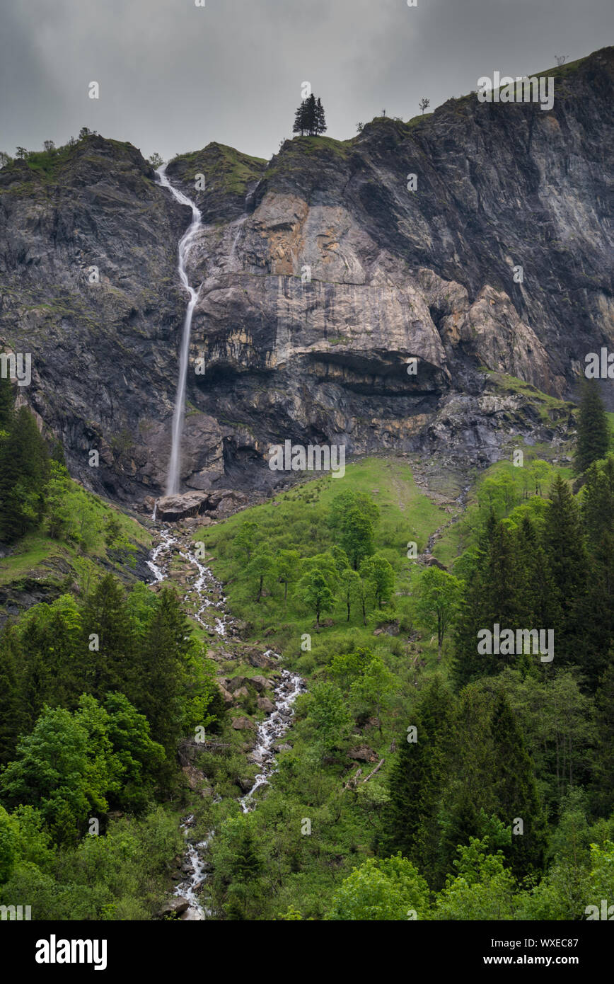high waterfall plummets off a rock and grass cliff in the Swiss Alps ...