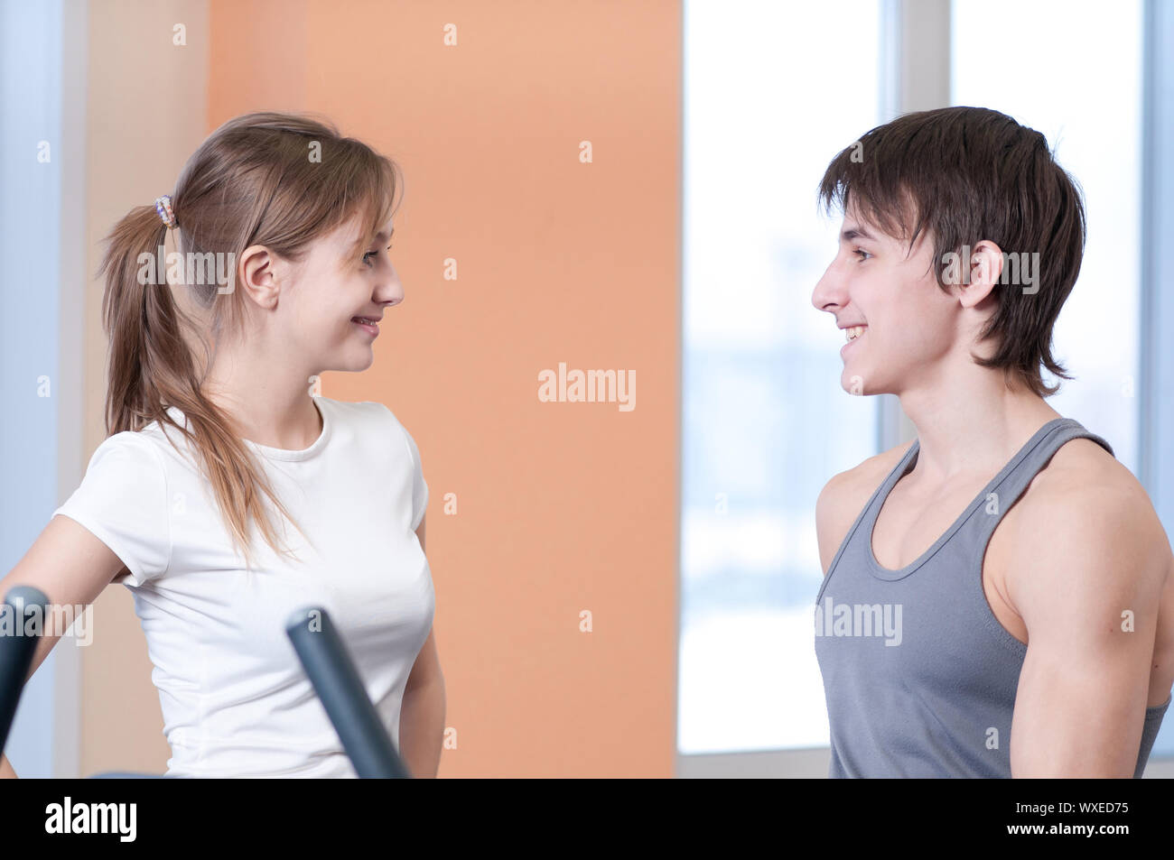 Woman and man train on machine in a gym assisted by personal instructor ...