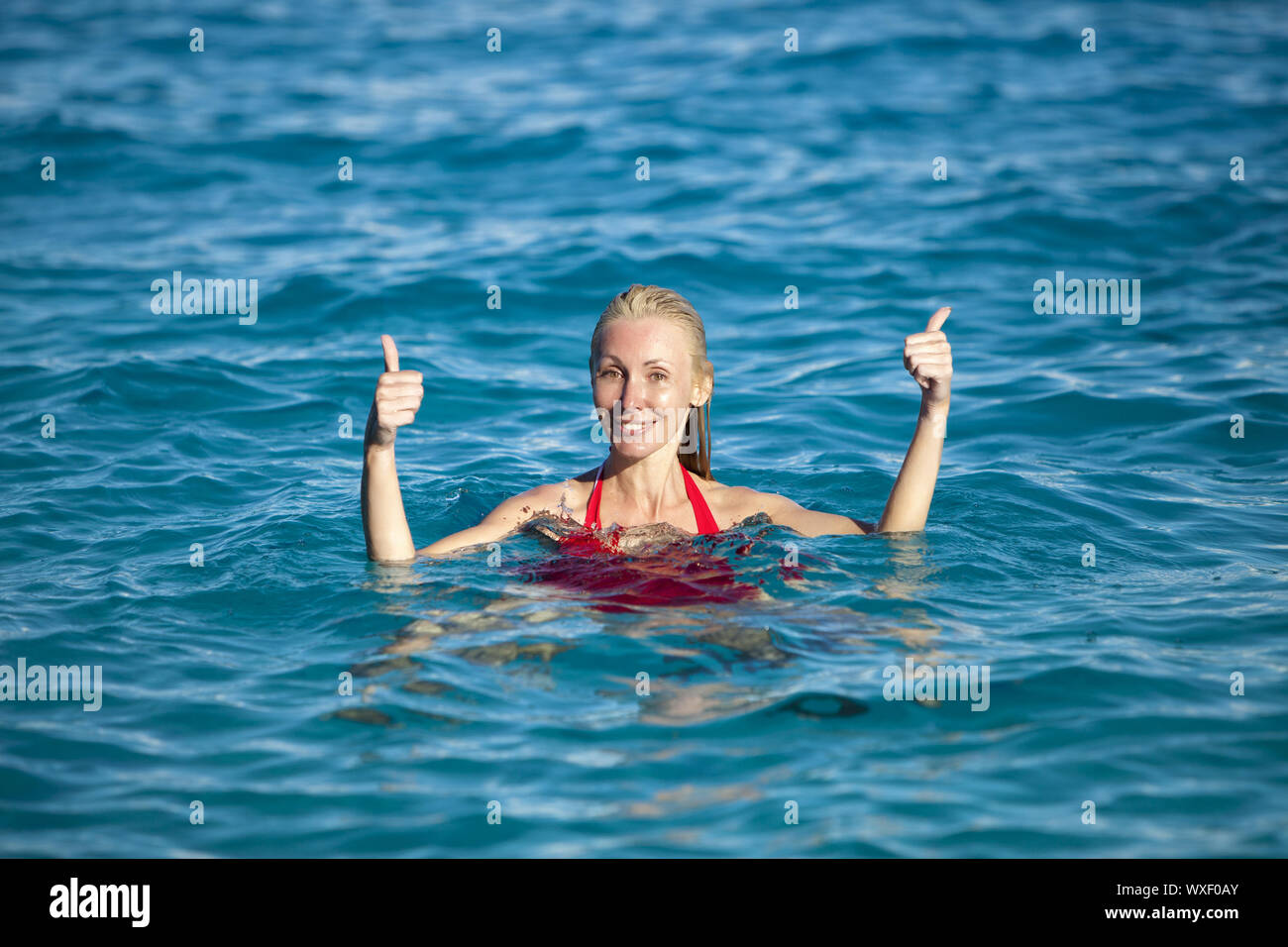 The young woman in a red bathing suit on sea background shows a thumb ...