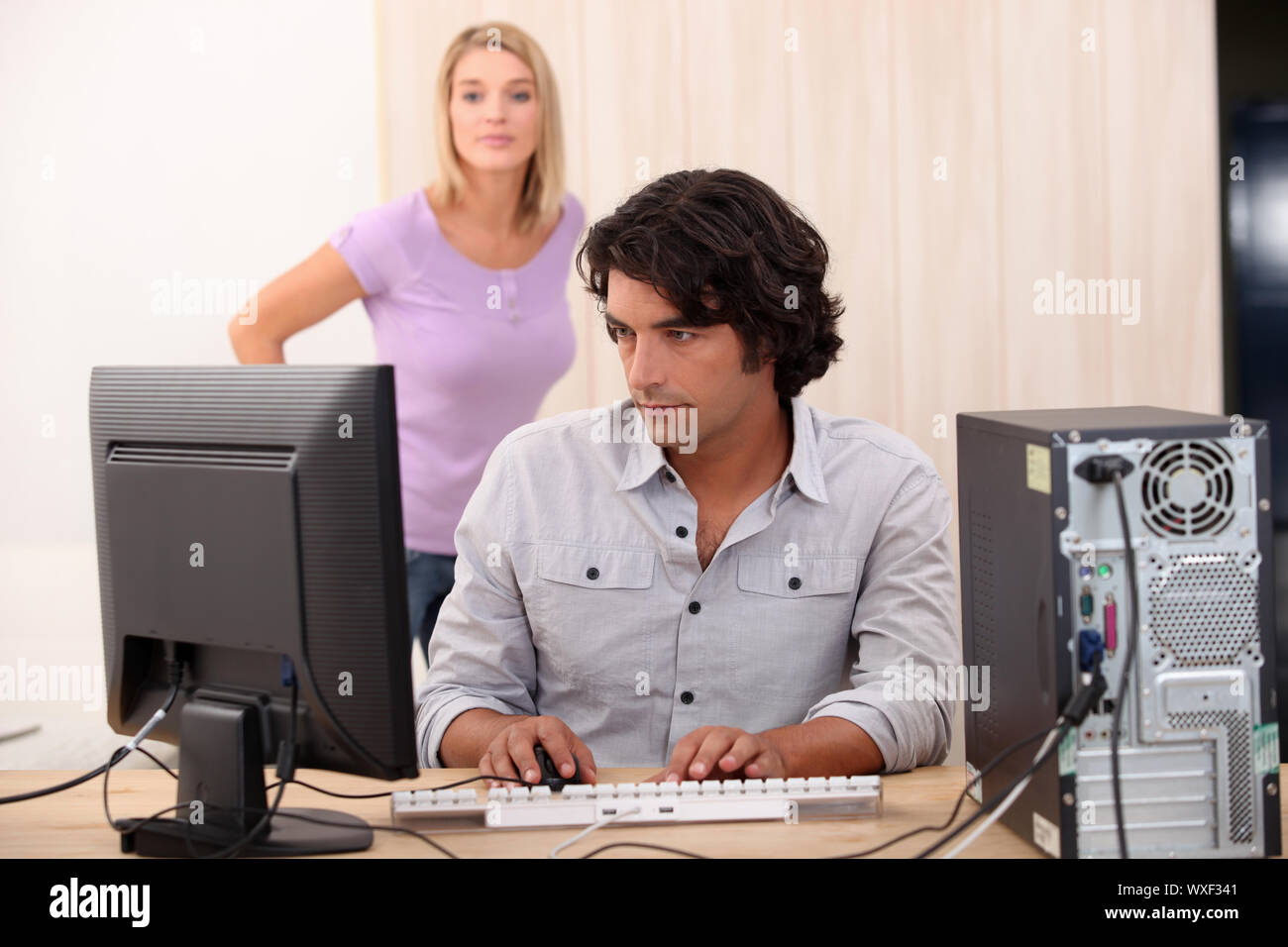 Male on his computer with his wife in the back Stock Photo - Alamy