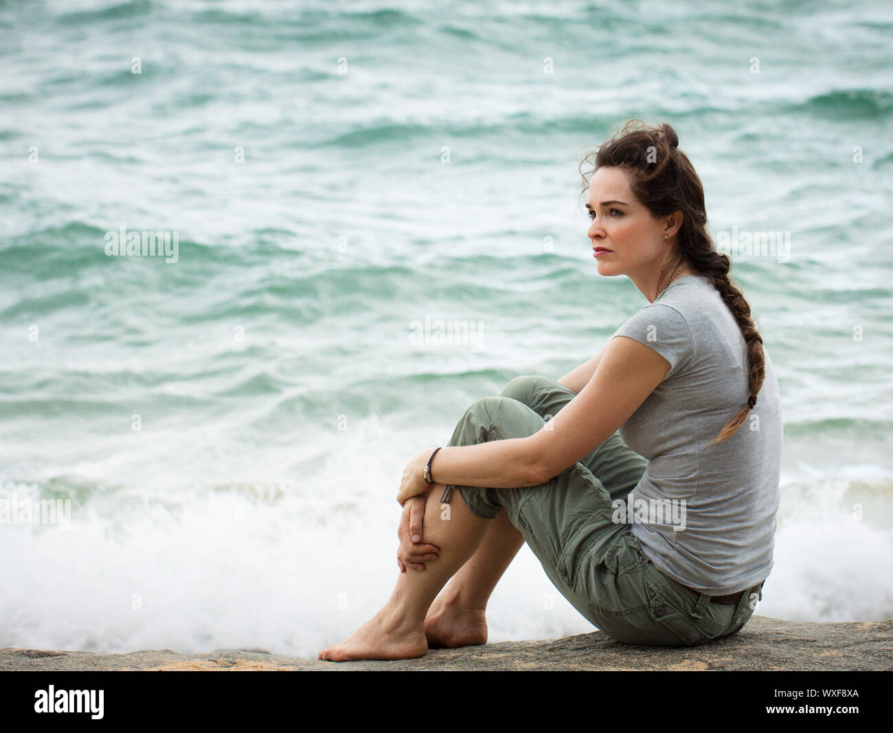 A sad and pensive woman sitting by the ocean deep in thought Stock ...