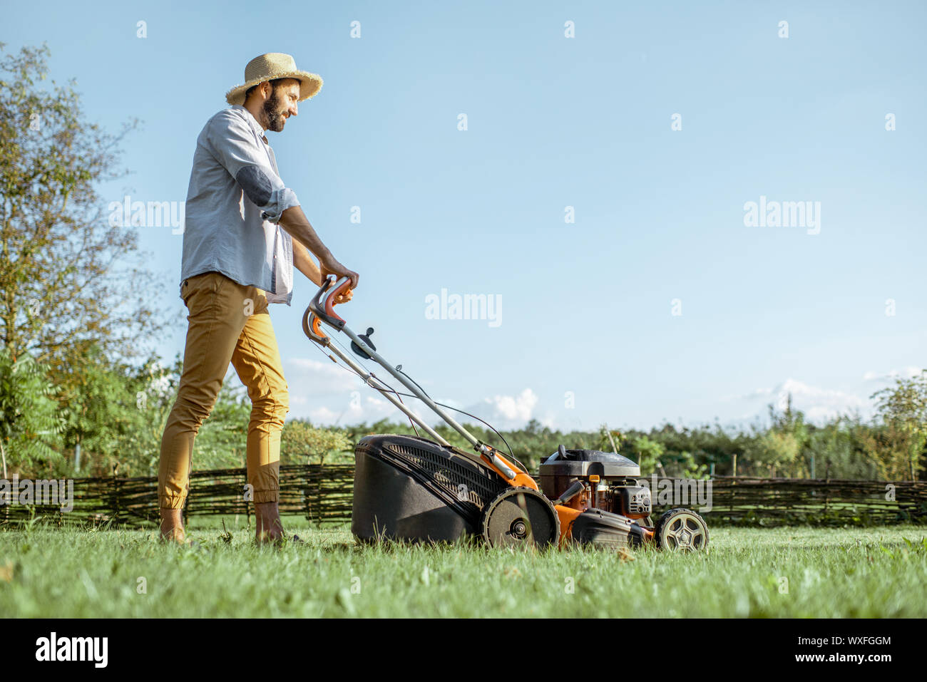 Handsome man dressed casually cutting grass with gasoline lawn mower ...