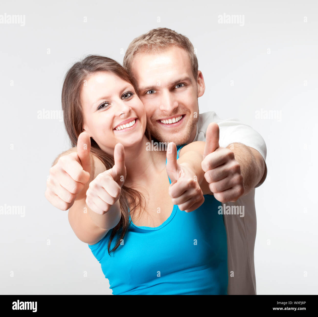 young couple showing both thumbs up smiling- isolated on gray Stock ...
