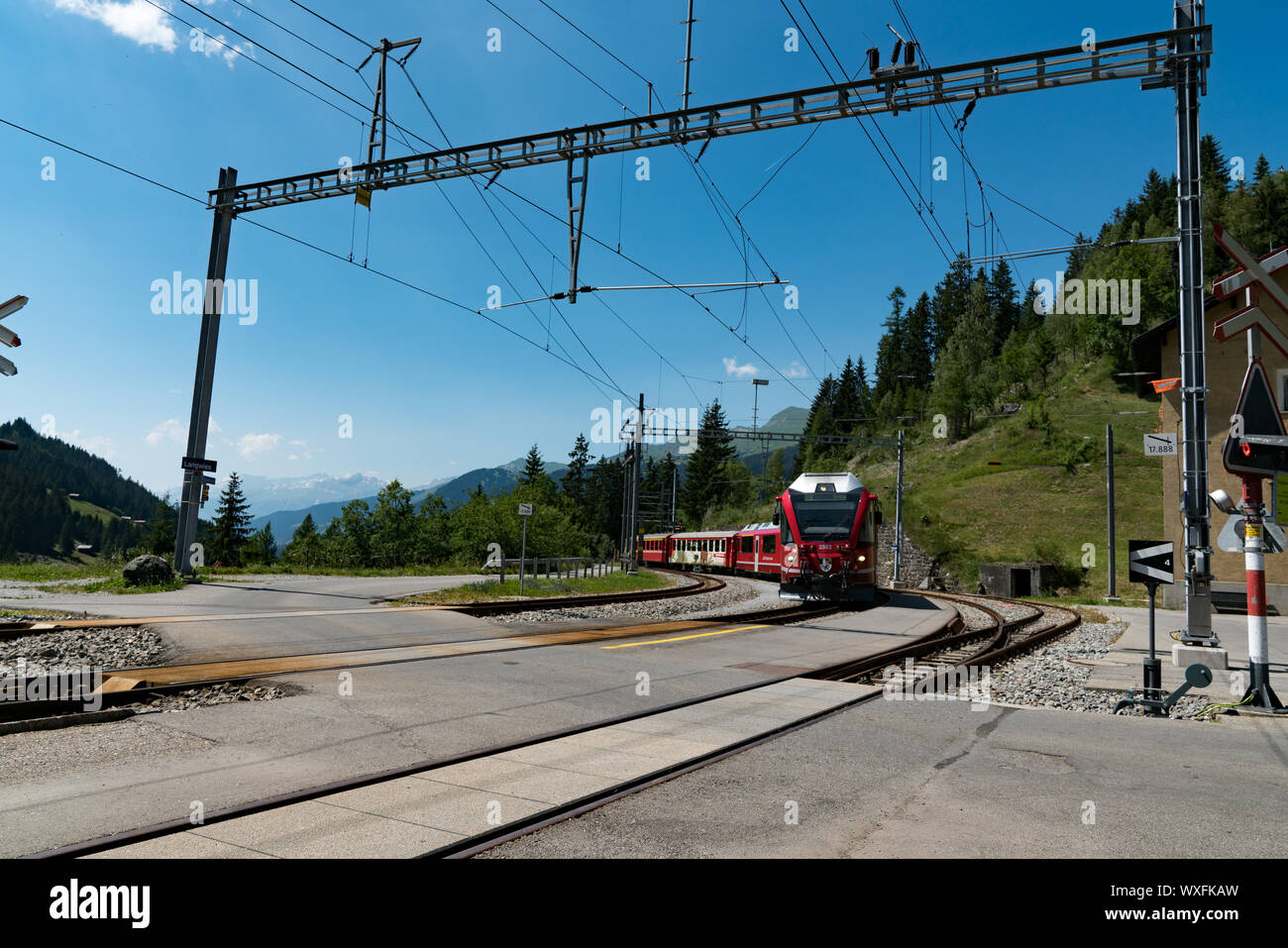 red narrow gauge train arrives at a remote train station in the Swiss ...