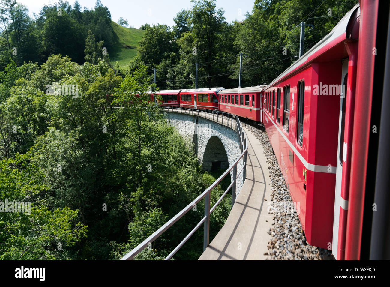 red narrow gauge traincrossing over a stone bridge on a curvy stretch ...