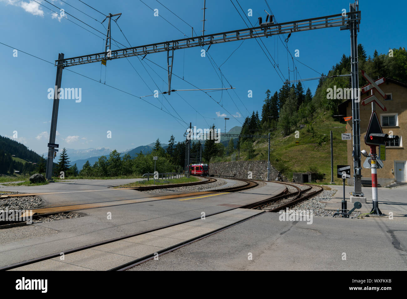 red narrow gauge train arrives at a remote train station in the Swiss ...