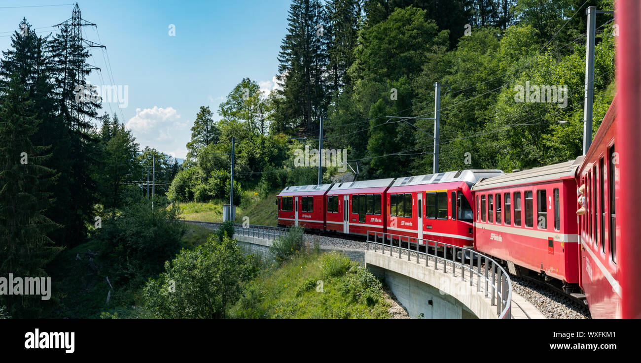 red narrow gauge traincrossing over a stone bridge on a curvy stretch ...