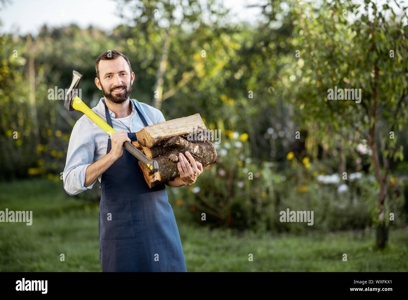 Portrait of a handsome lumberman standing with axe and wood on the ...