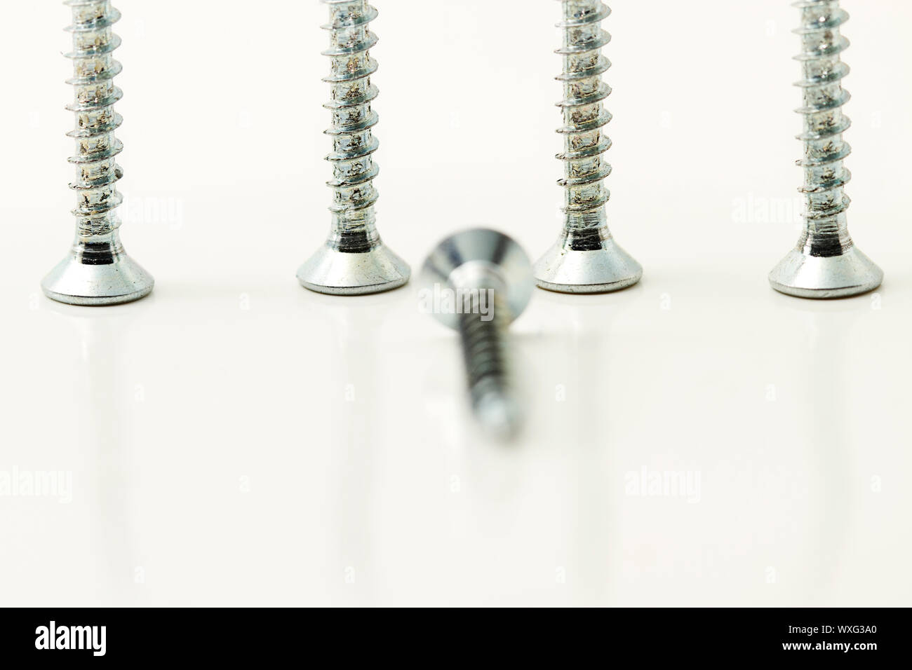 four screws standing behind one screw on white background Stock Photo ...