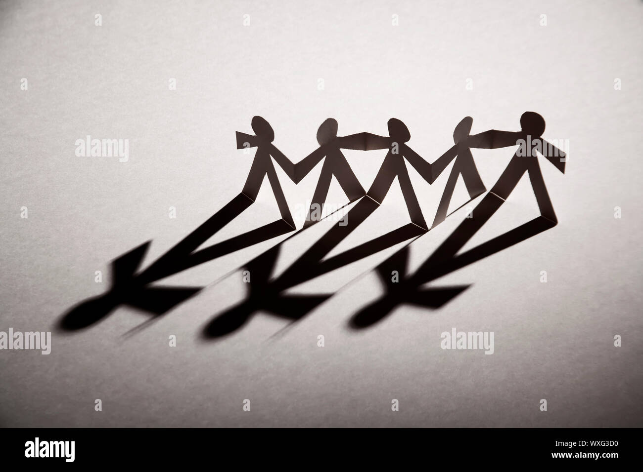 Line of cutout paper dolls throwing a shadow Stock Photo - Alamy