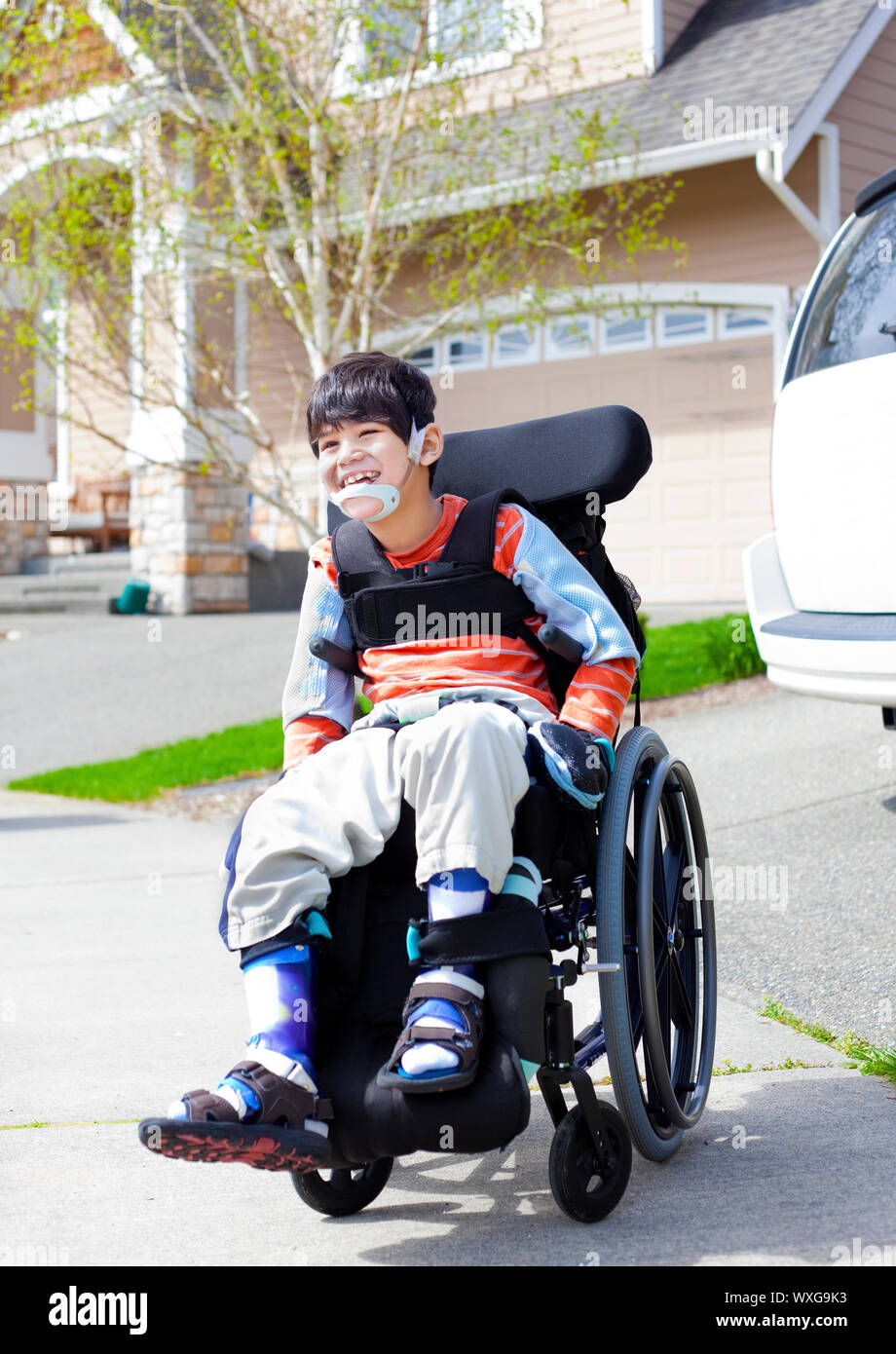 Happy disabled six year old boy waiting on sidewalk in wheelchair ...