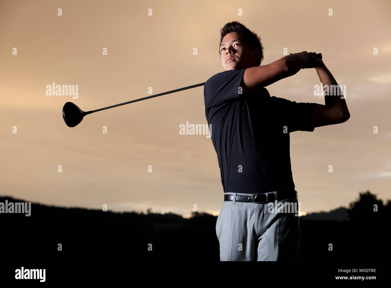 Golf player teeing off at sunset Stock Photo - Alamy