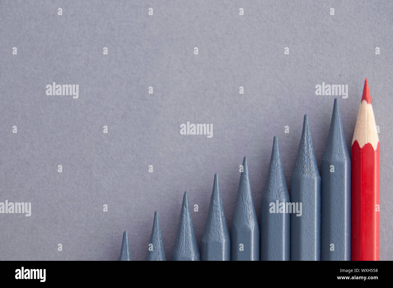 Red pencil amongst greyed out pencils conceptual Stock Photo - Alamy