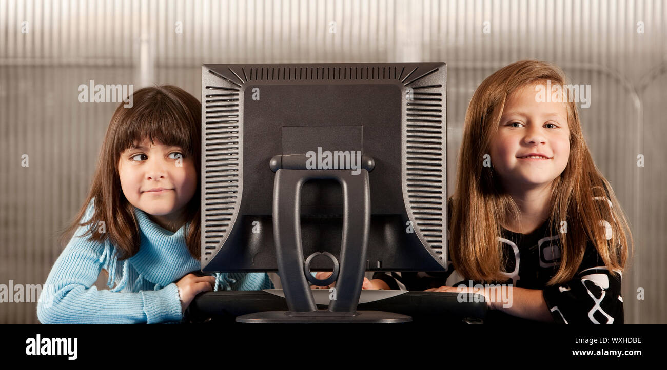 Two young girls looking from behind computer monitor Stock Photo - Alamy