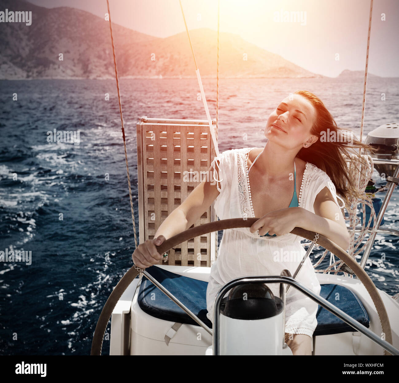 Woman behind the wheel yacht, enjoying sea nature and mountais ...