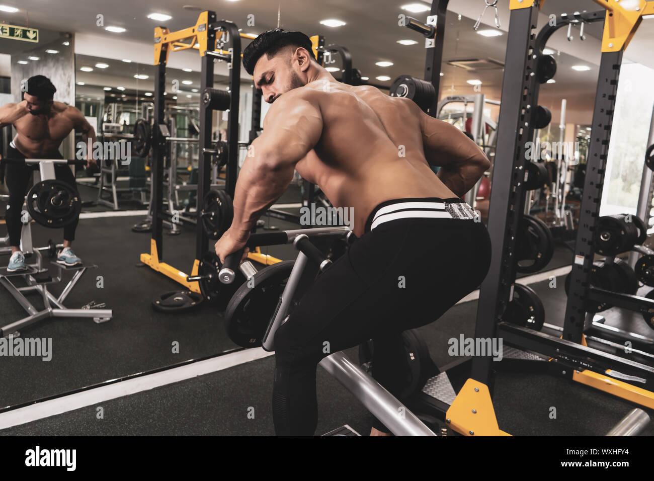 Muscular men exercising with weights. He is performing T bar rows for ...