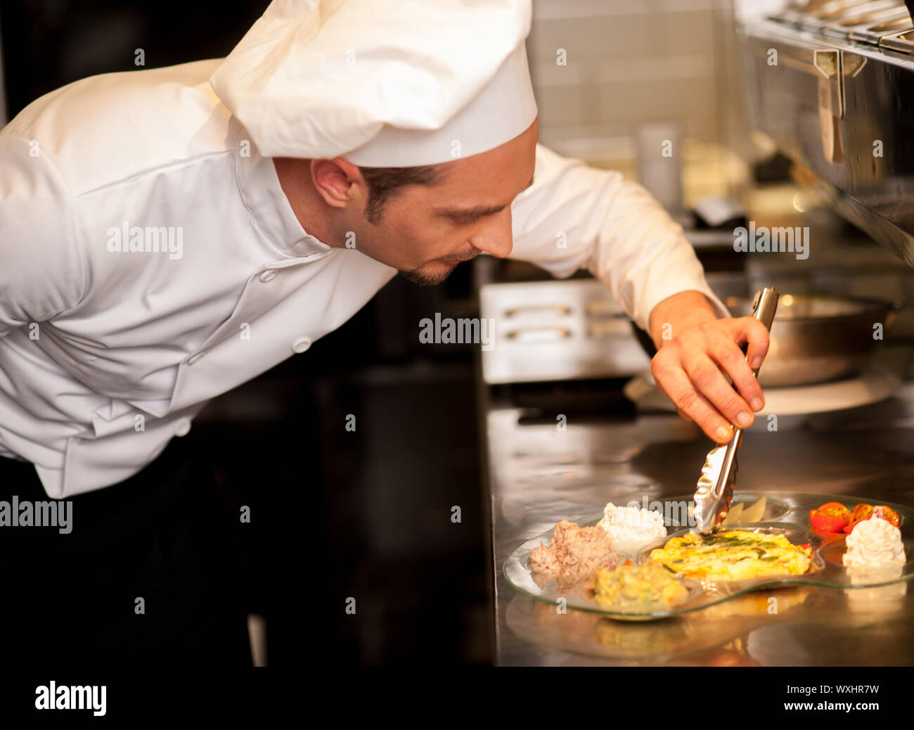 A chef placing food with help of a tong on final meal-plate Stock Photo ...