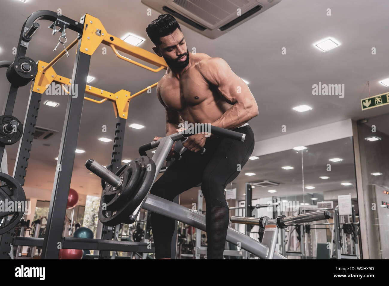Muscular men exercising with weights. He is performing T bar rows for ...
