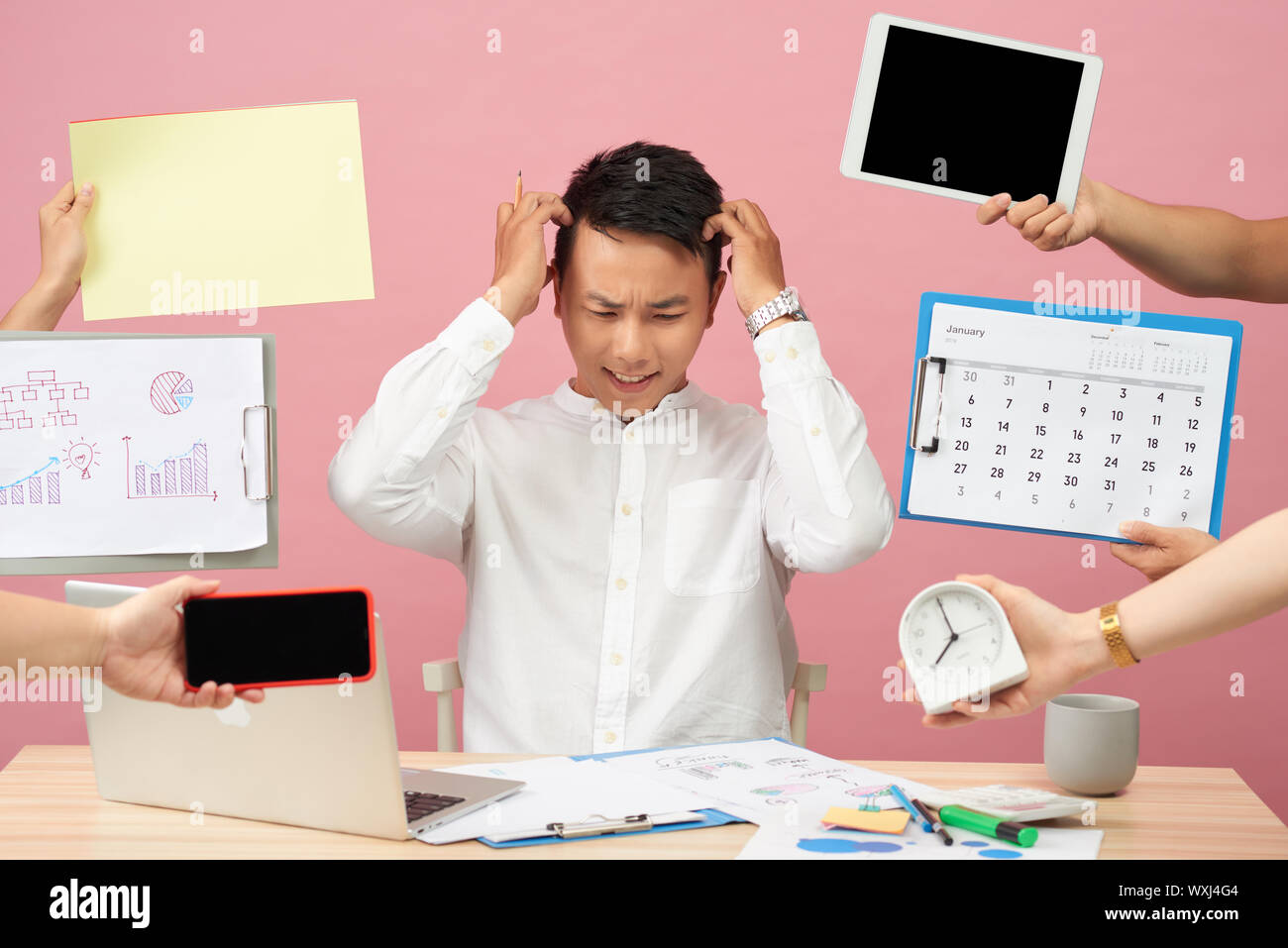 Sad young man sits at desktop, hands with papers, alarm clock, touchpad ...