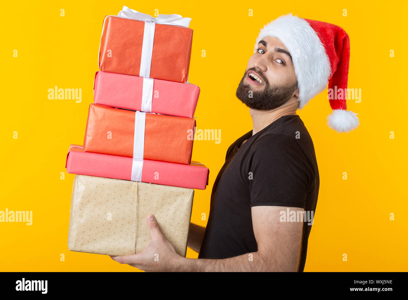 Disgruntled young man with a beard in a Santa Claus hat holds five gift ...