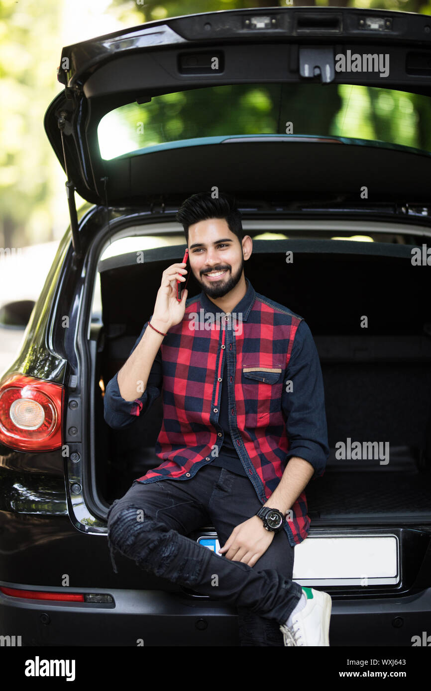 Young indian man talking on the phone while sitting in the trunk of his ...