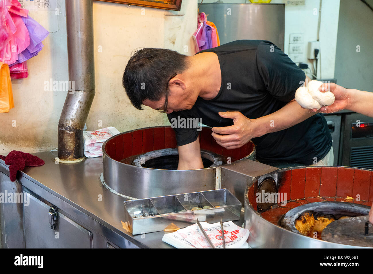 Taipei, Taiwan: Man sticking Pepper Pork Buns on wall inside a cylindrical clay oven. Hu Jiao ...