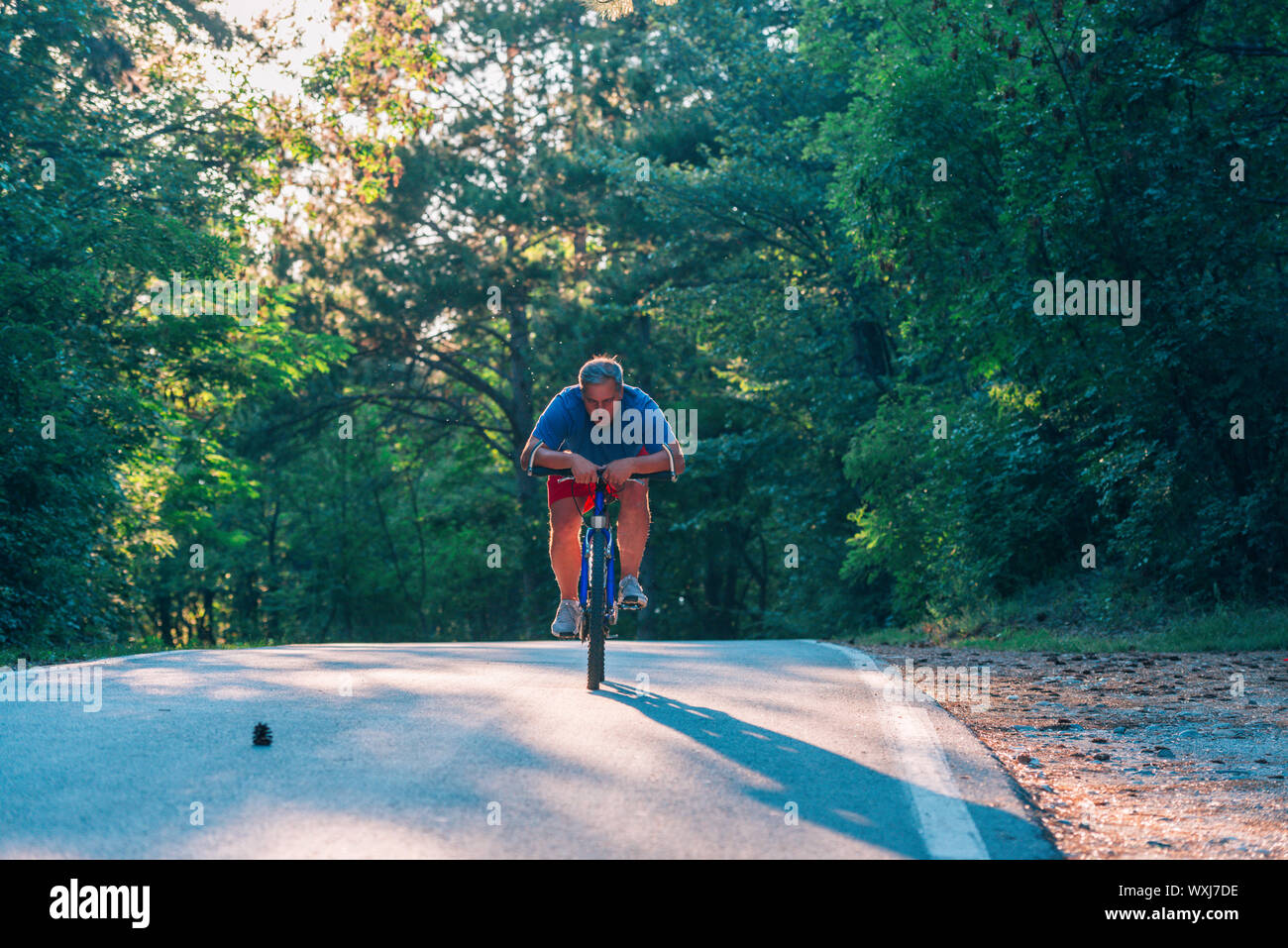 Older cyclist in his mid-40s riding a bike on a road through the woods ...