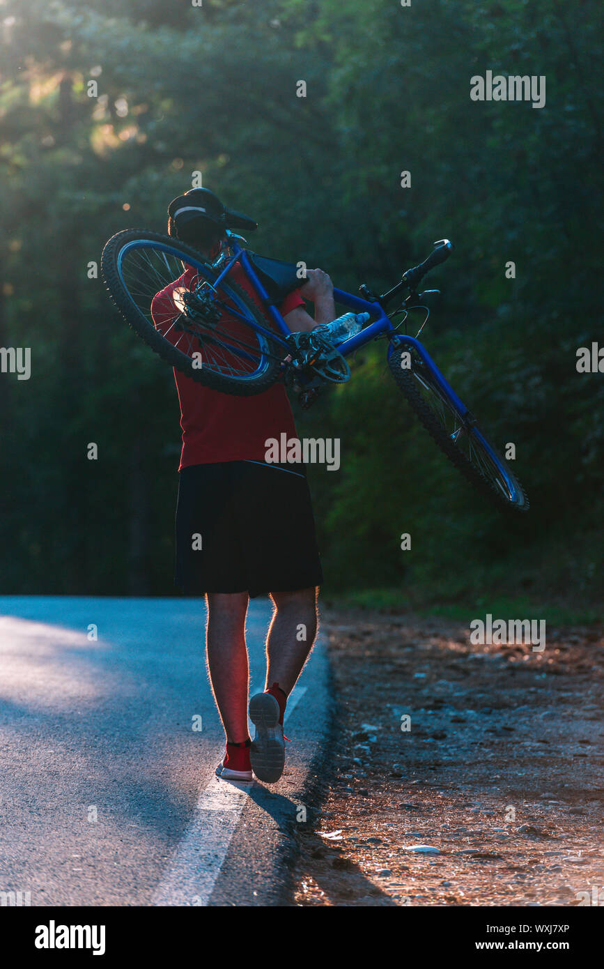 Strong athlete cyclist ( biker ) carrying his bicycle on his back on an ...