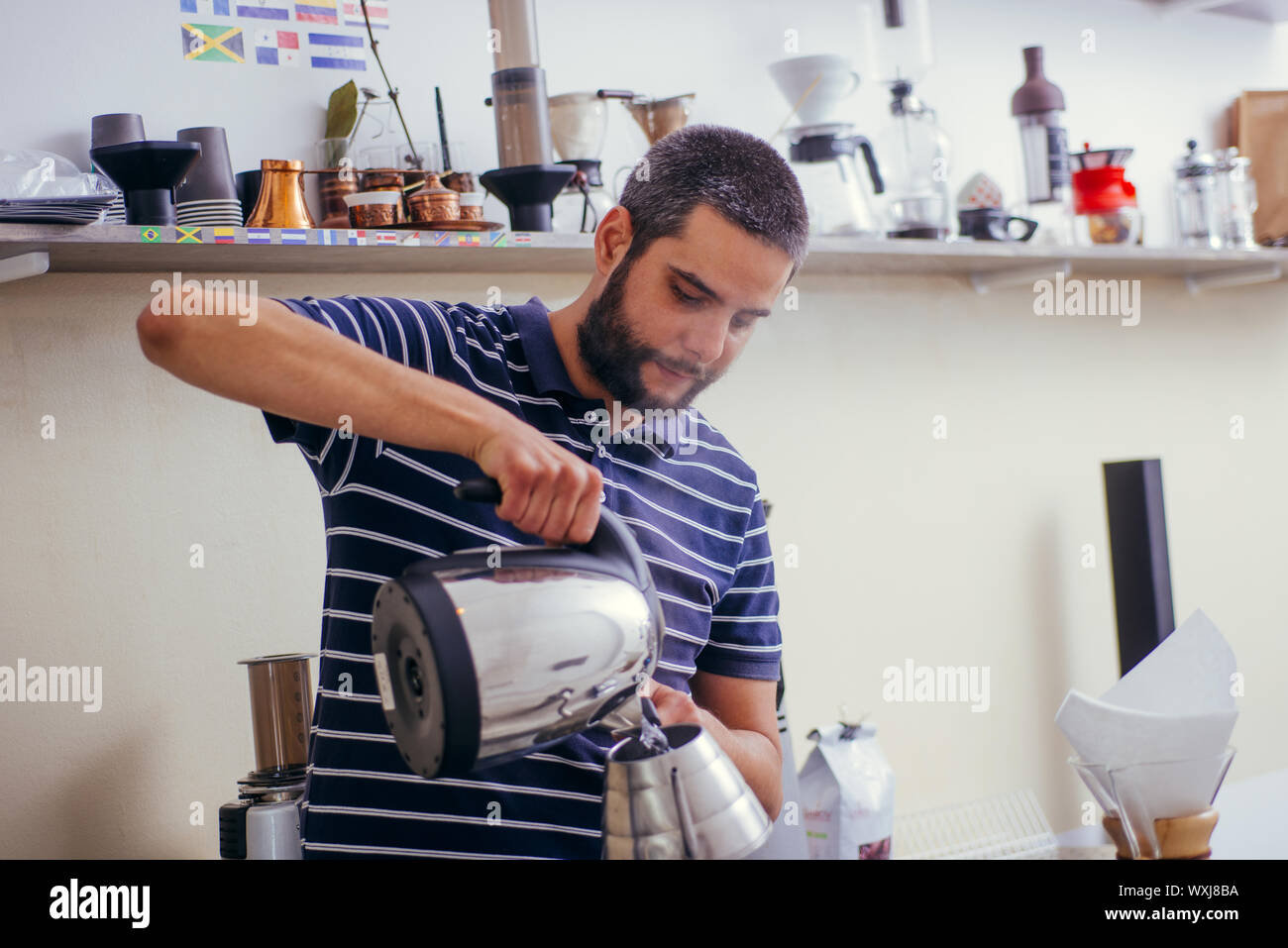 Indoor shot of young male barista making a cup of coffee while standing ...