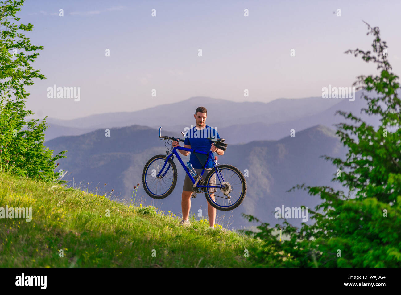 Tired cyclist is wiping his sweat off his face while pushing his ...