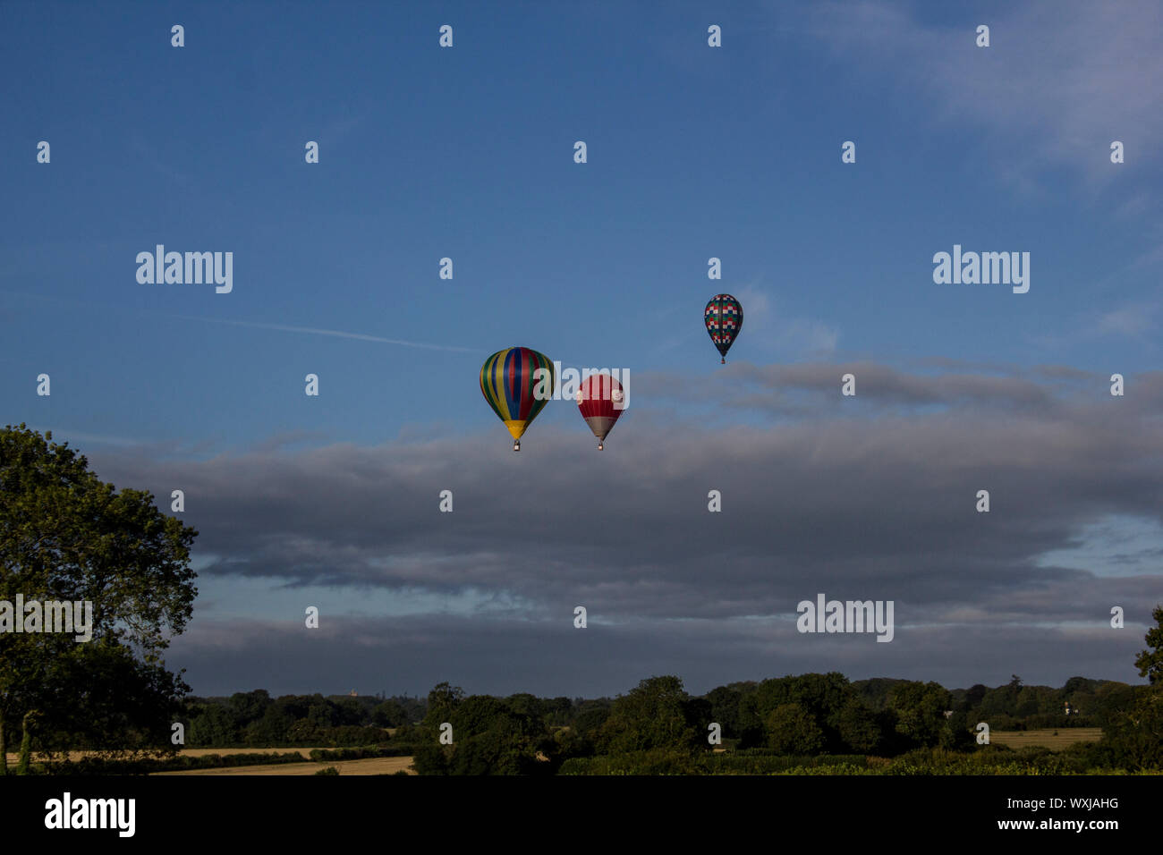 Three hot air balloons flying over the English countryside with a few ...