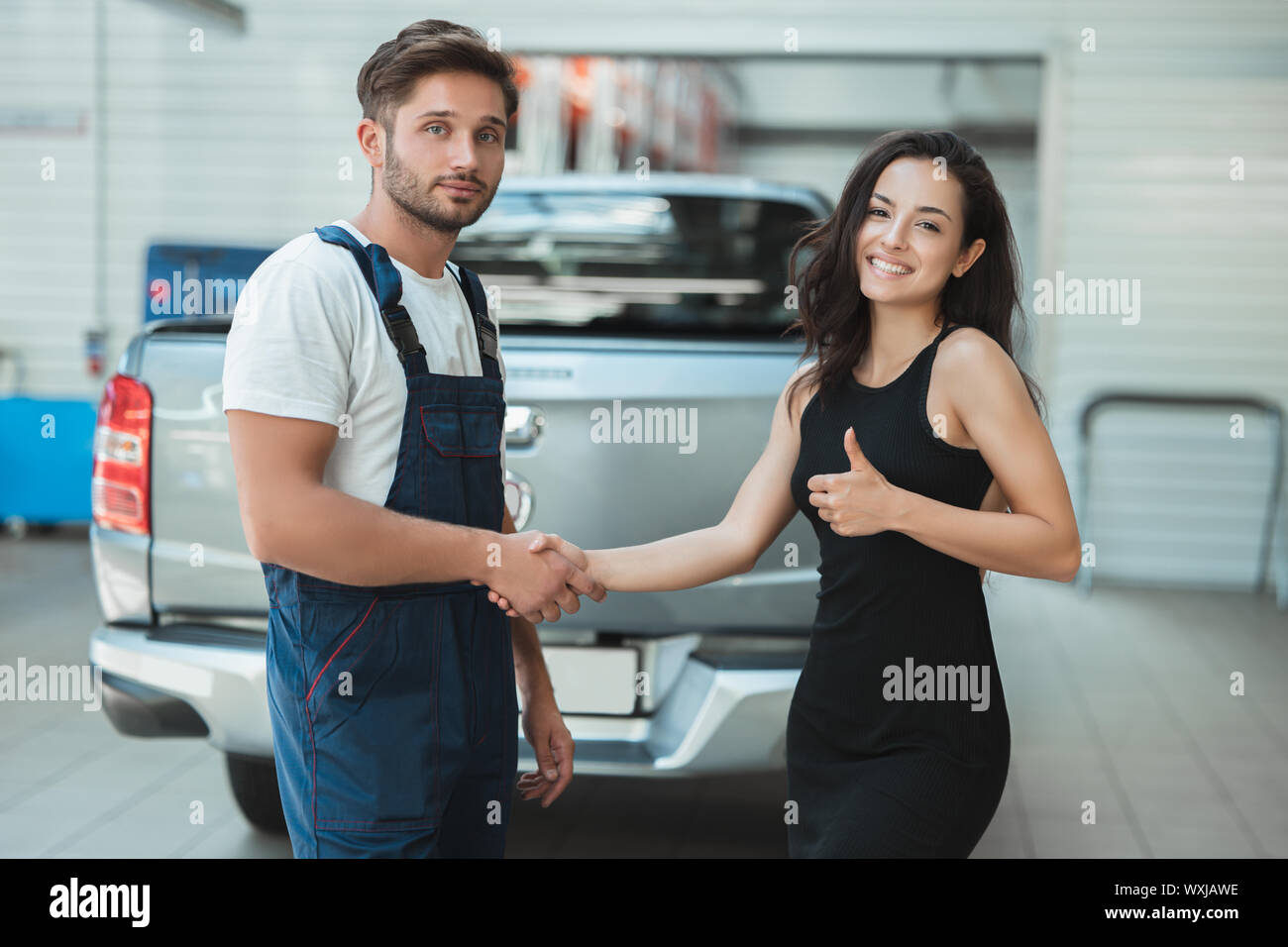 young handsome smiling mechanic and beautiful woman client shaking ...