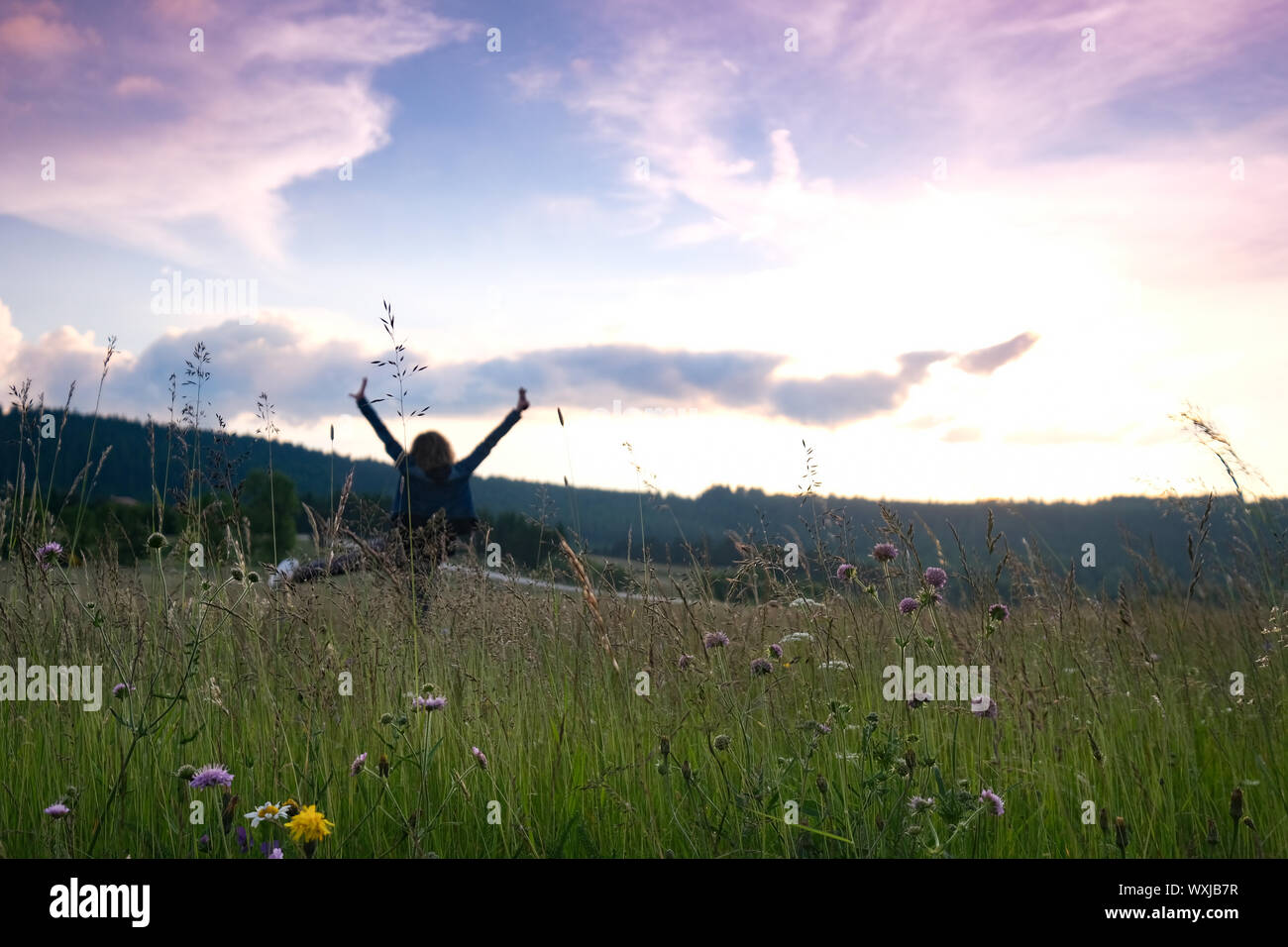 Rear view of a woman standing in a field with her arms in the air ...