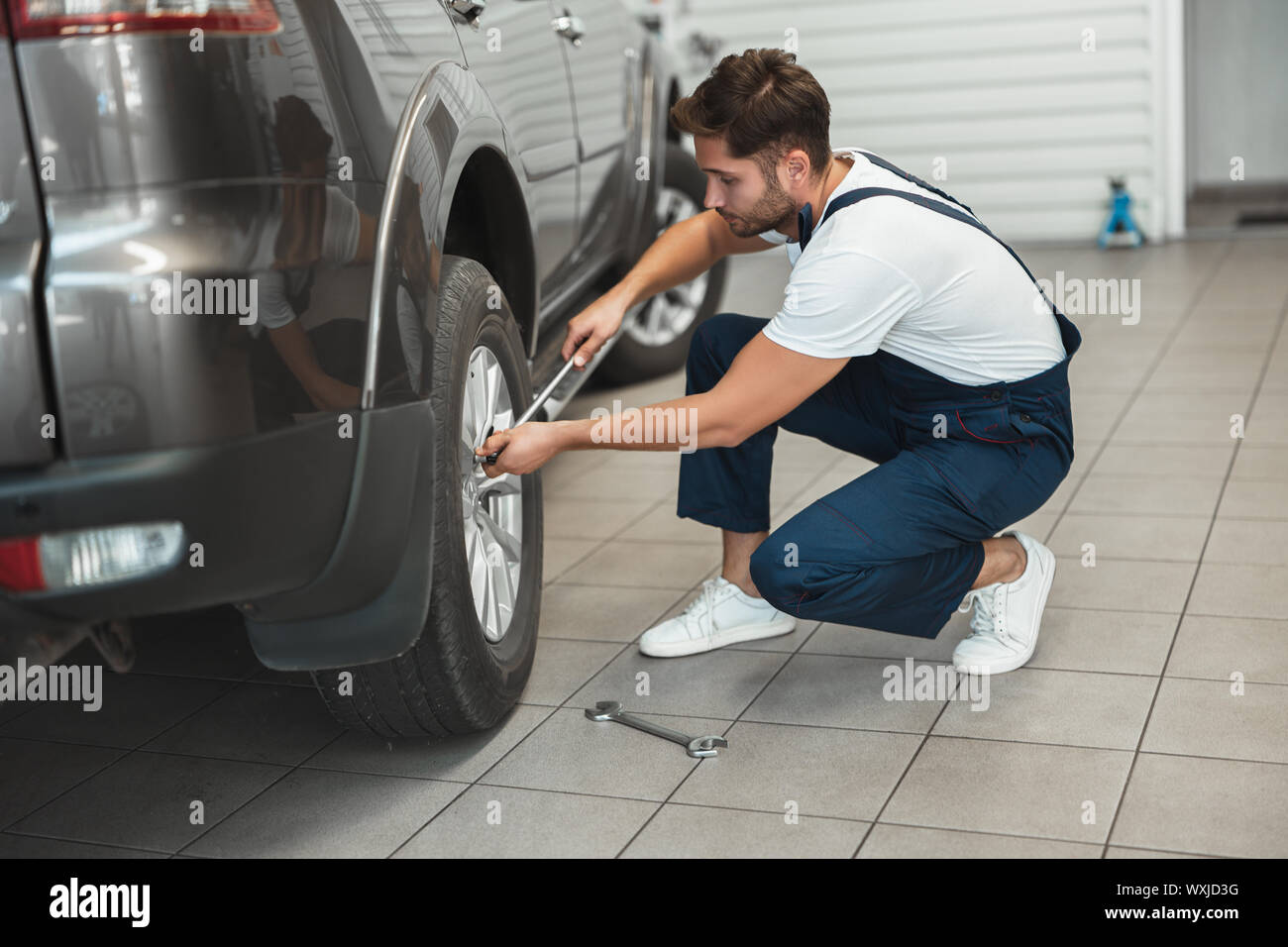 young handsome mechanic wearing uniform working in car service ...