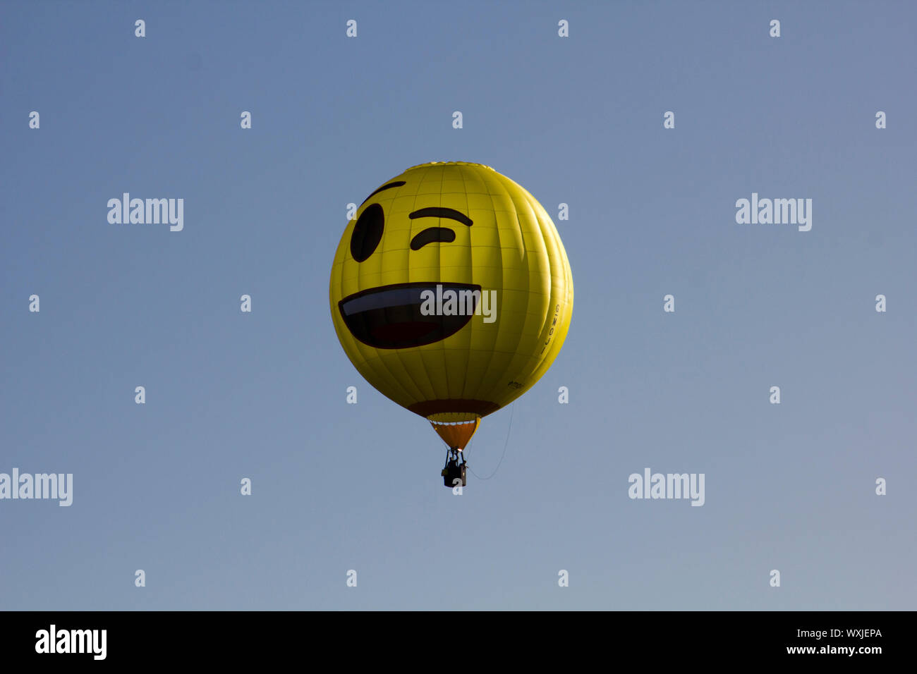 A yellow happy, winking emoji hot air balloon flying against a blue sky ...