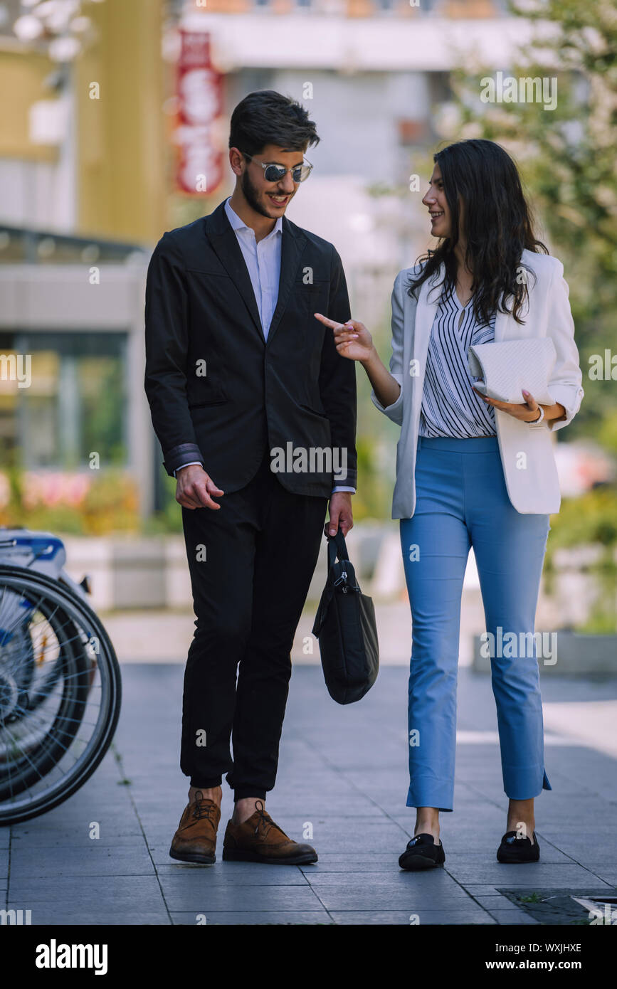 Happy Caucasian business colleagues walking outside office & talking to ...