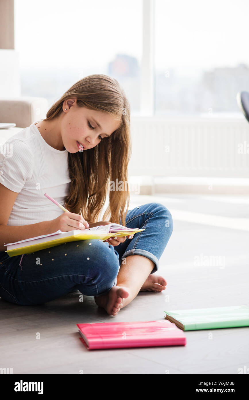 Girl writing or drawing in notebook sit on floor. Girl does homework at ...