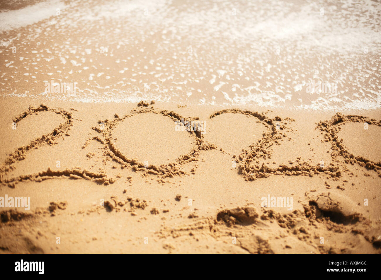 2020 New Year. 2020 written on sandy beach with wave foam at sea beach ...