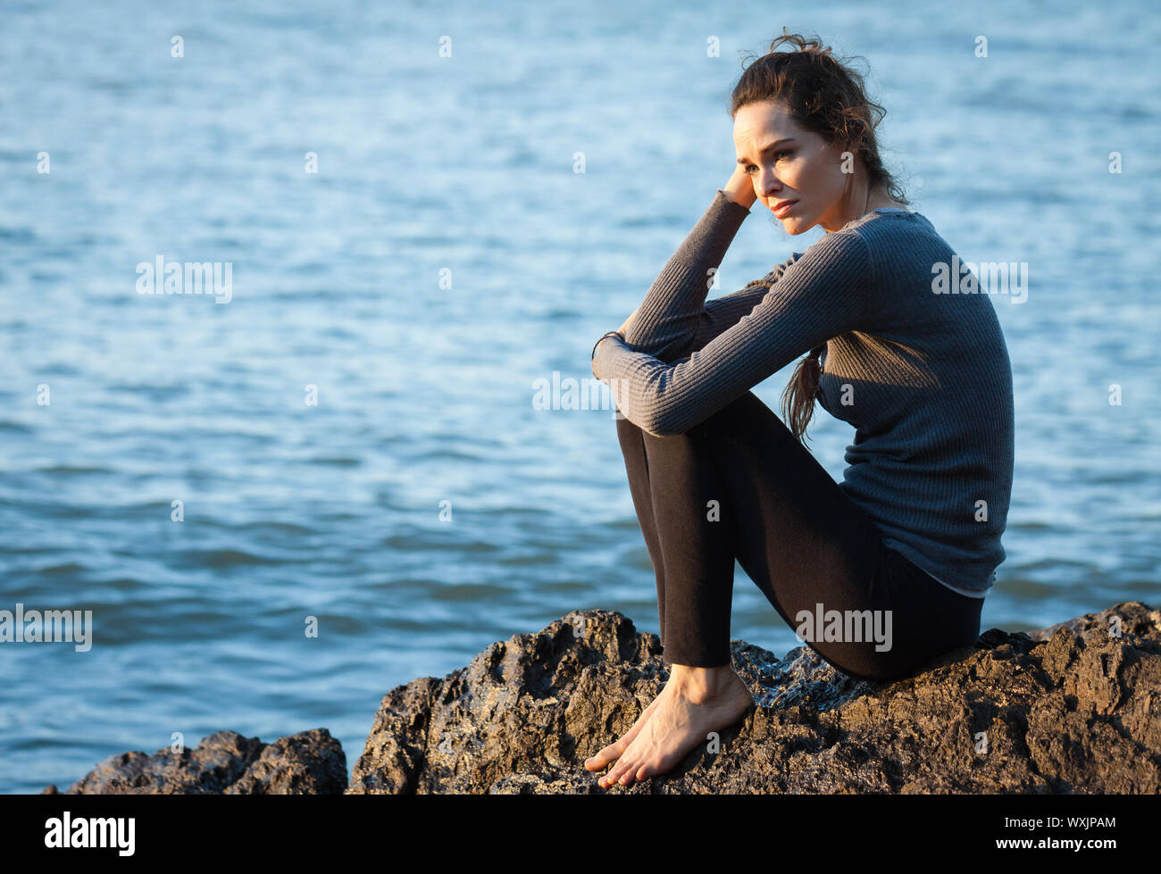 Sad and depressed woman sitting by the ocean Stock Photo - Alamy